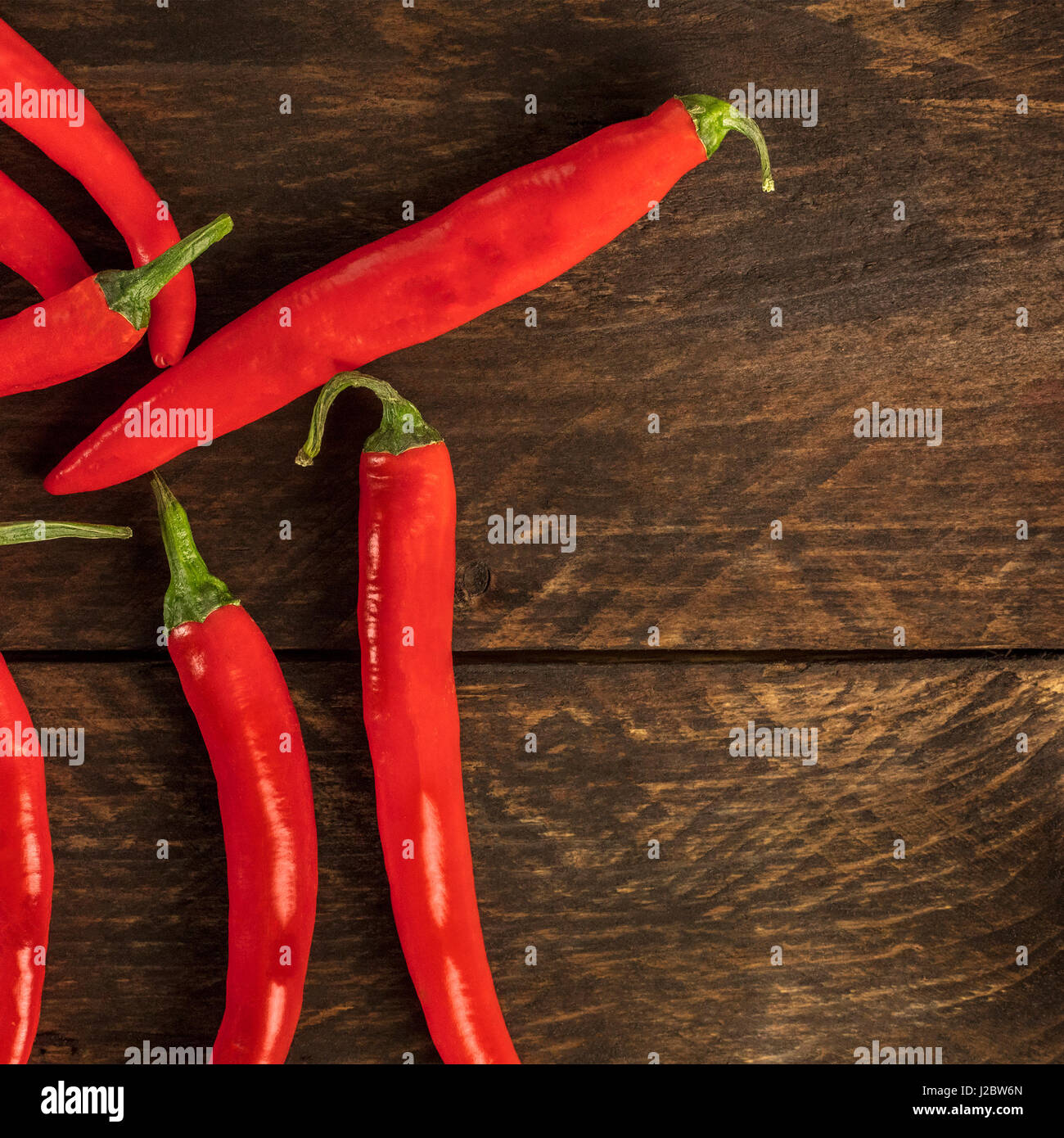 A square photo of red hot chili peppers, shot from above on a dark ...