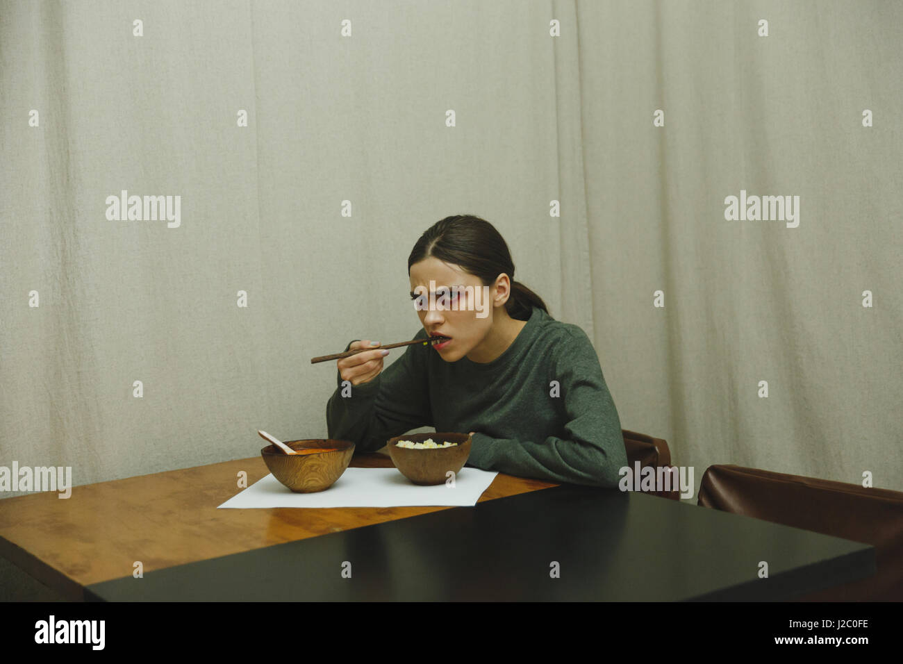 Side view of a serious woman in sweater eating by the table while being ...