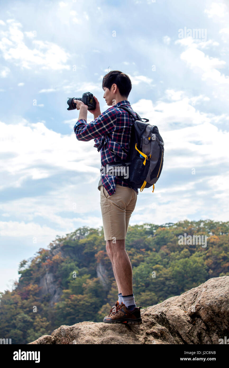 Side view of male trekker with camera standing on a rock Stock Photo ...