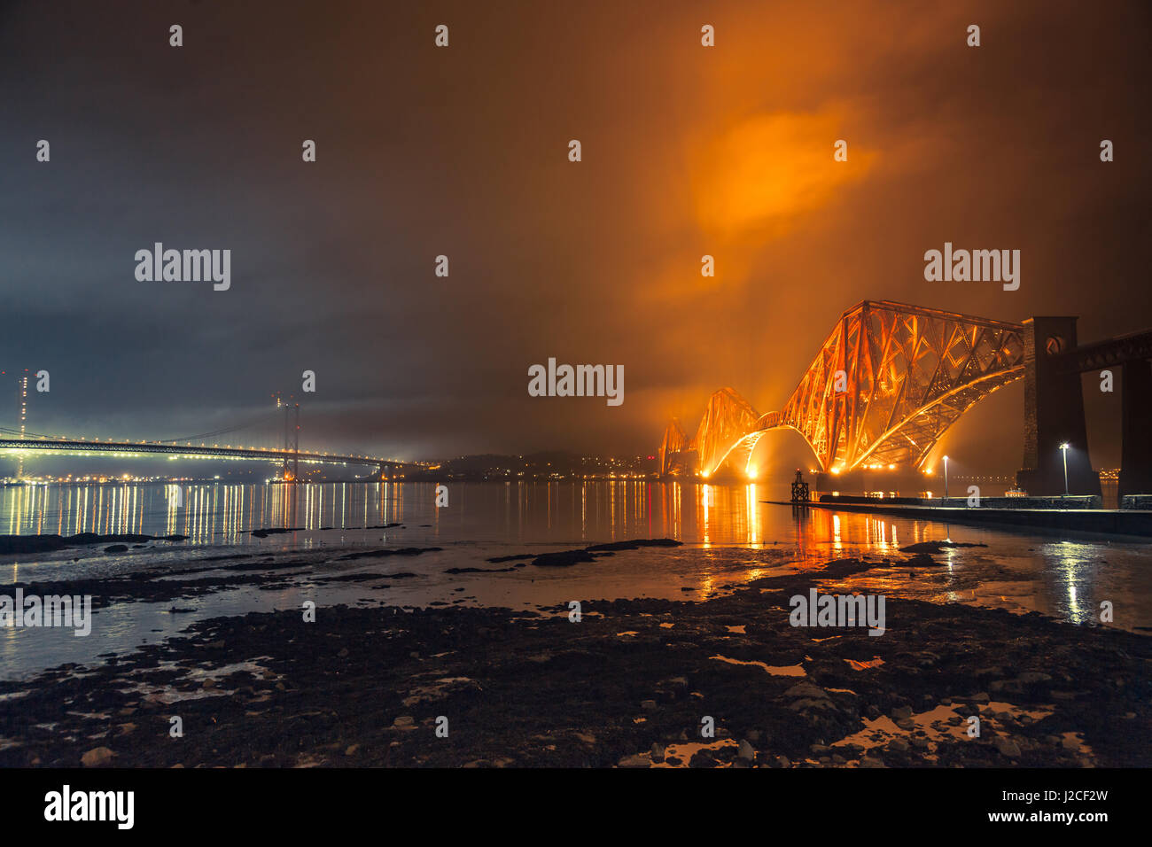 The Forth Rail Bridge lit up at night. Golden light hits the clouds ...
