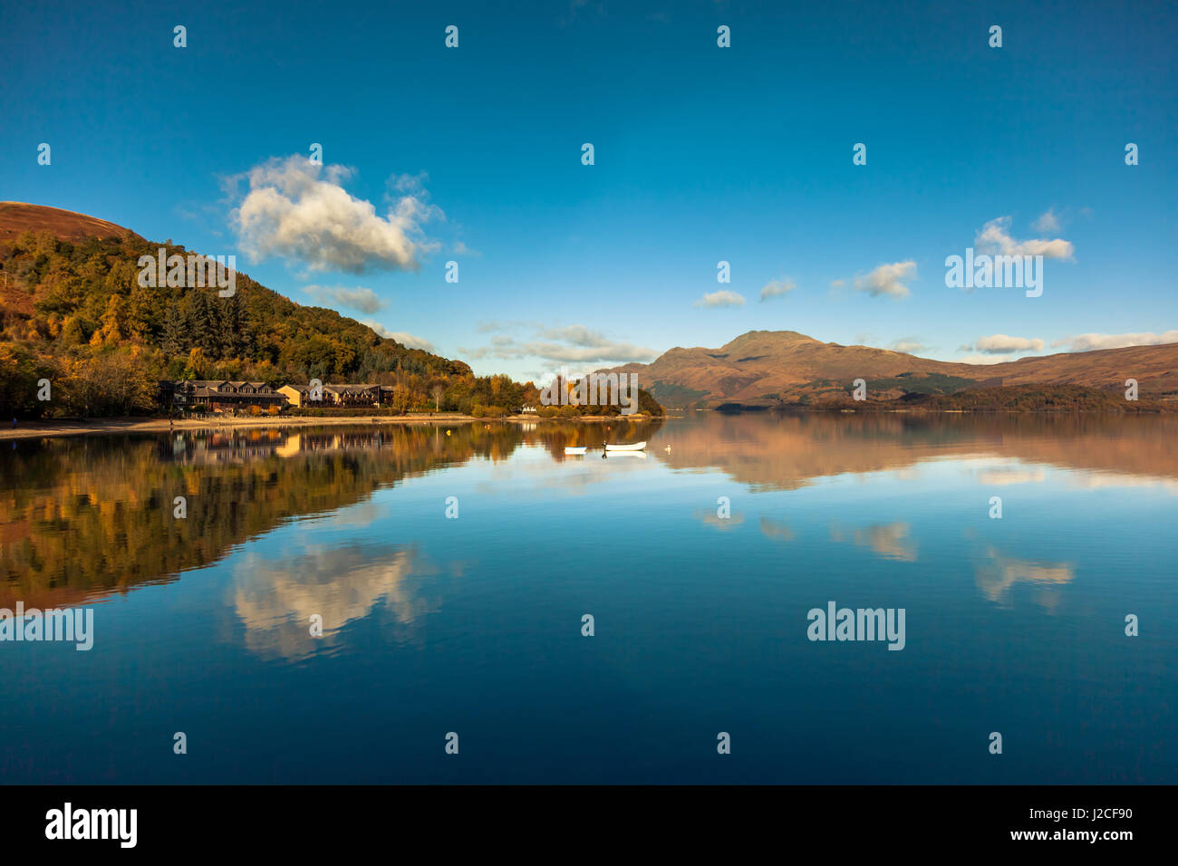 Clouds reflect in the calm waters of Loch Lomond on a clear sunny day ...