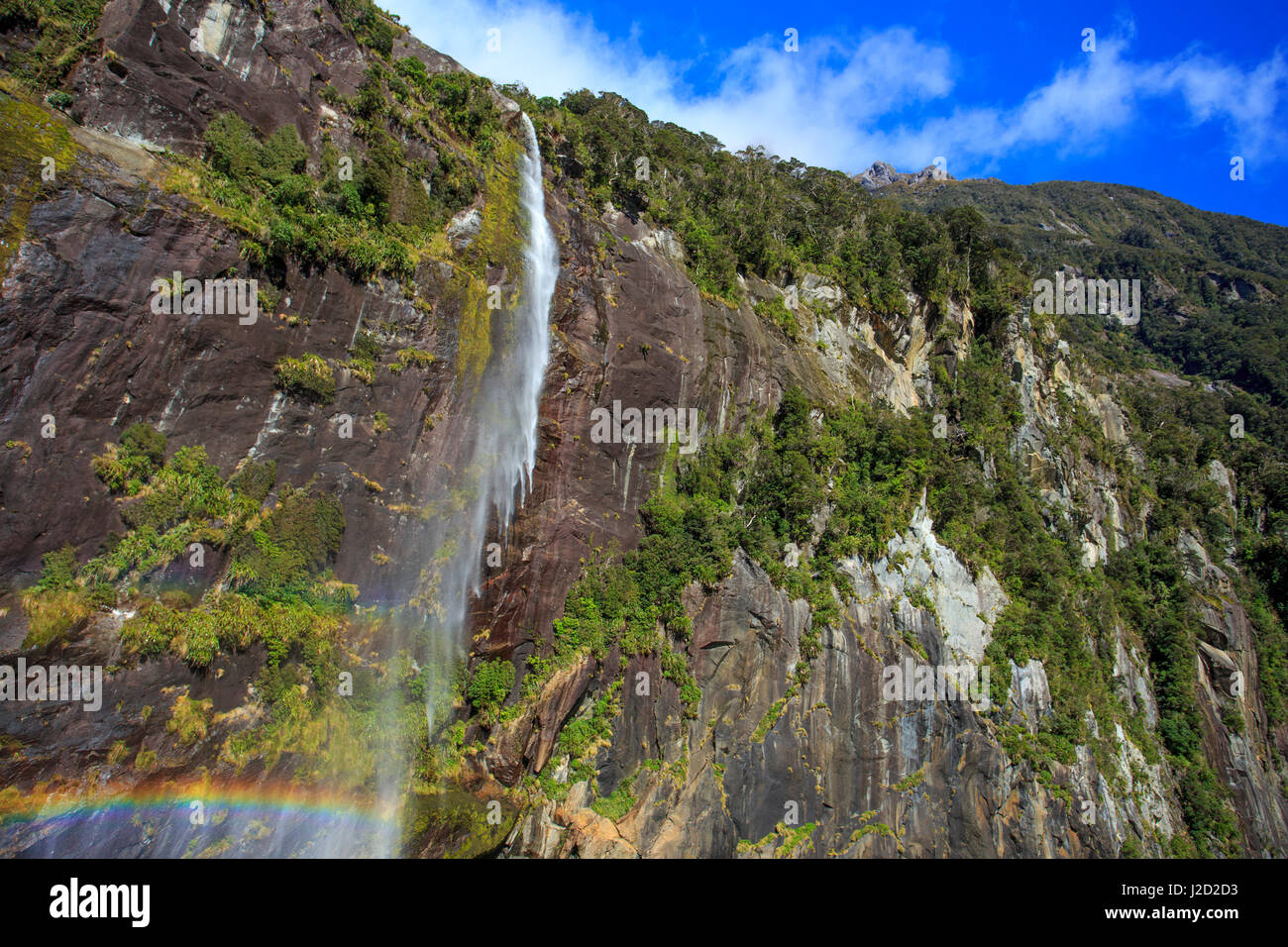 A tall waterfall drops off a steep cliff into the waters of Milford ...