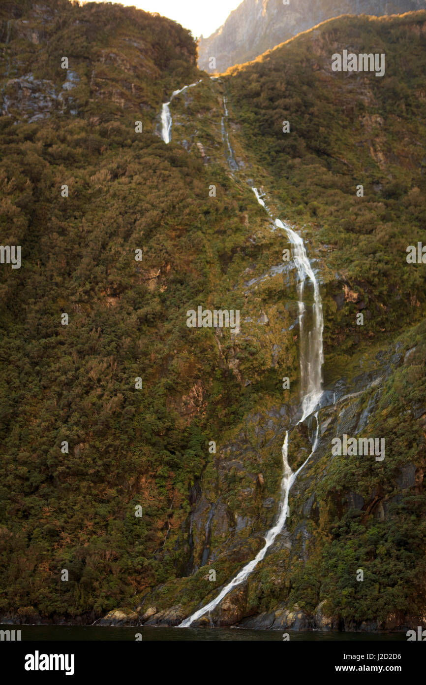 A tall waterfall drops off a steep cliff into the waters of Milford ...