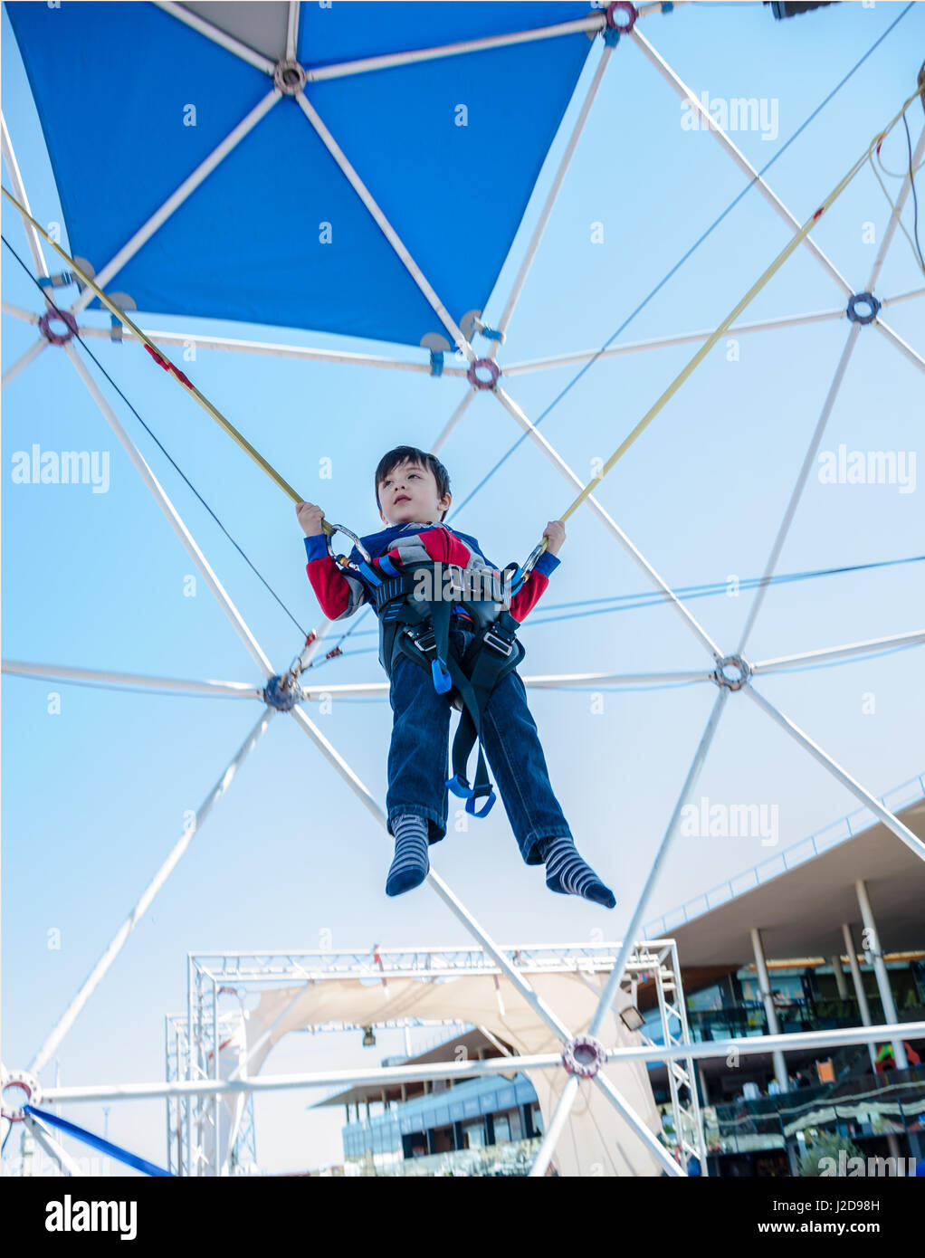 A young boy bouncing on a trampoline with bungie ropes attached to help ...