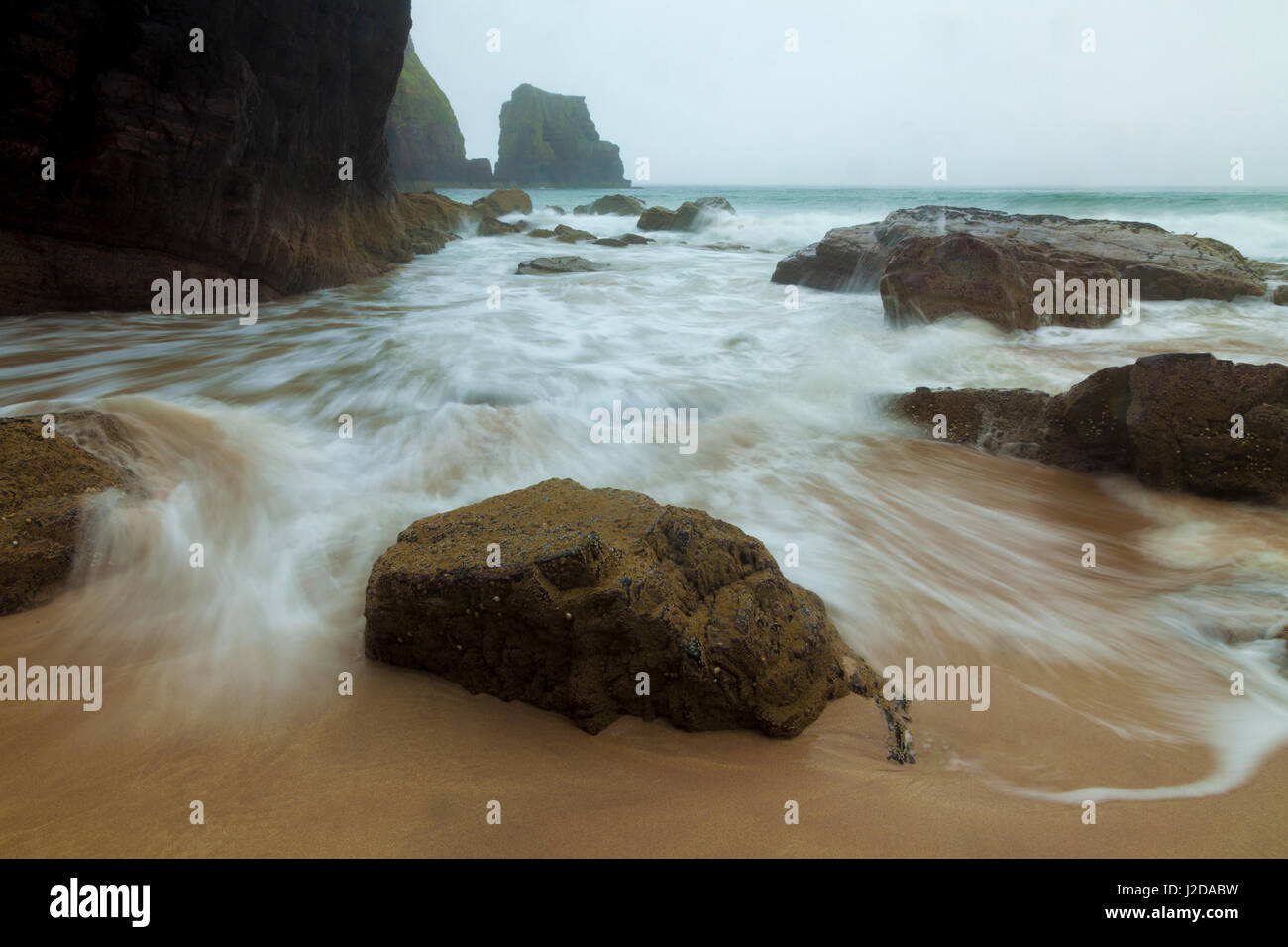 a wave of the rising tide washes over the beach and the rocks beneath ...