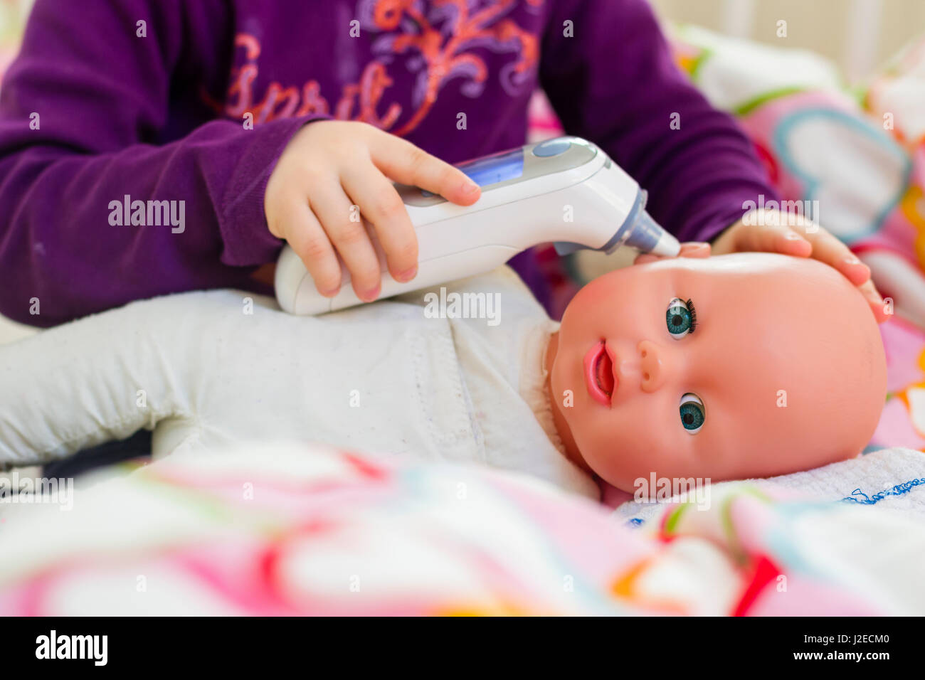 Little girl playing doctor with a doll, measuring temperature with ...