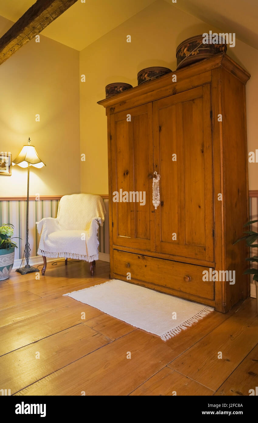 White throw over sitting chair and antique wooden armoire in master ...