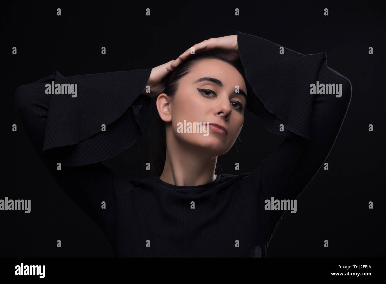 one young adult woman, black clothes head face, black background studio ...