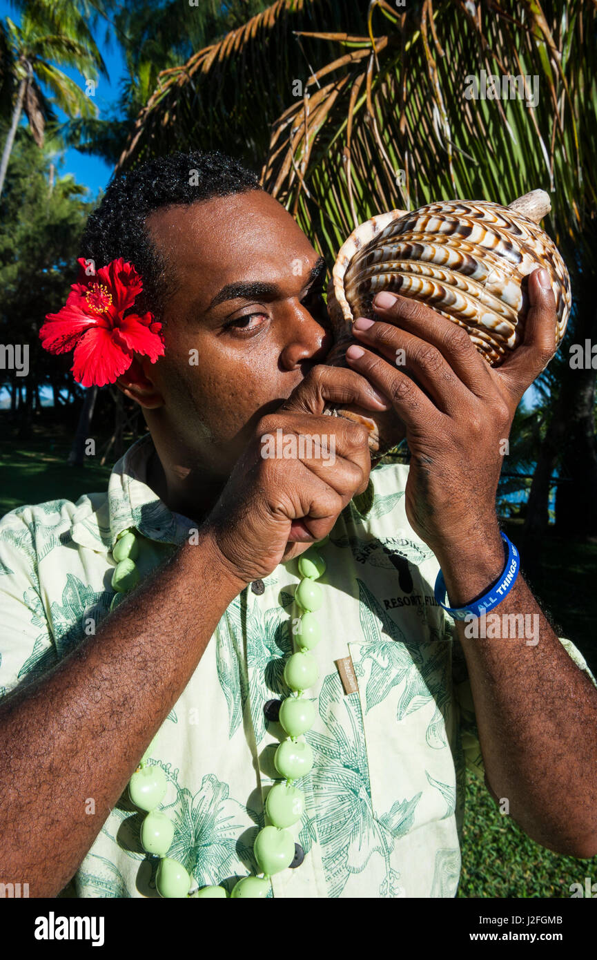 Local Fijian man blowing on a huge shell, Safe Landing Resort, Nacula ...