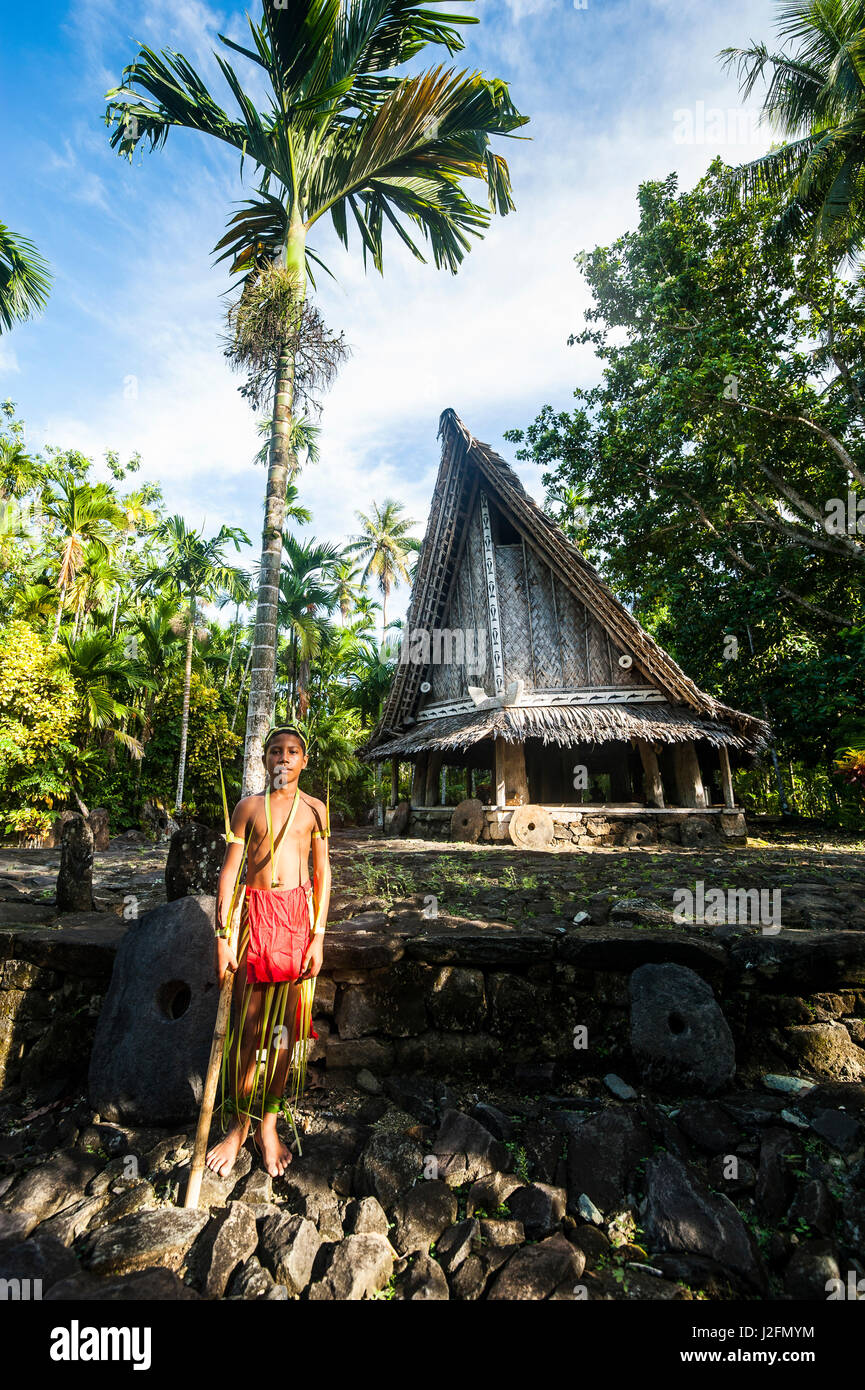 Young boy in traditional dress standing before a traditional hut on the ...