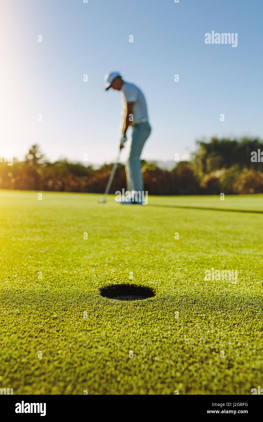 Vertical shot of golf hole in the green field with golfer in background ...