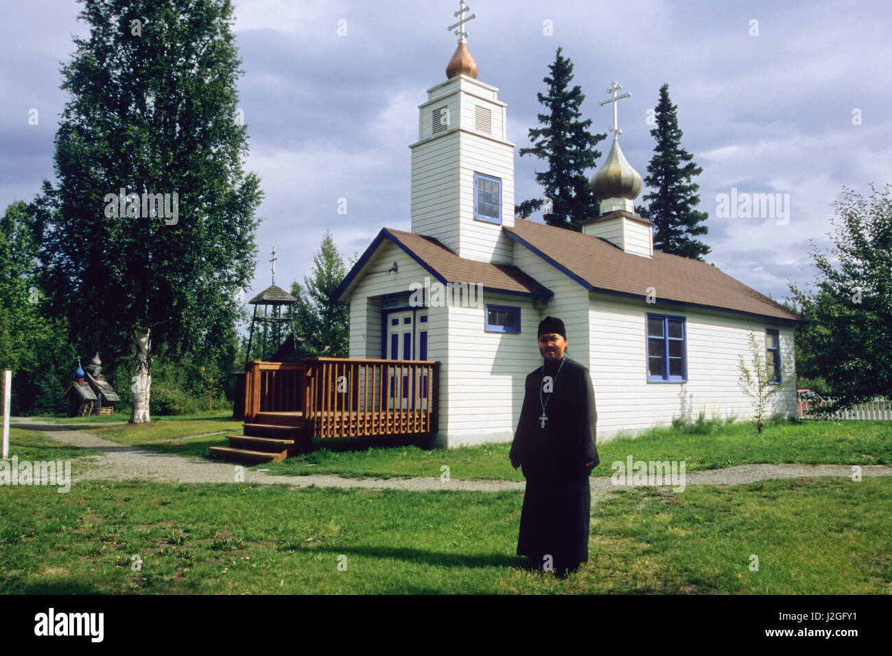 Alaskan Native man dressed in black robes of the parish stands in front ...