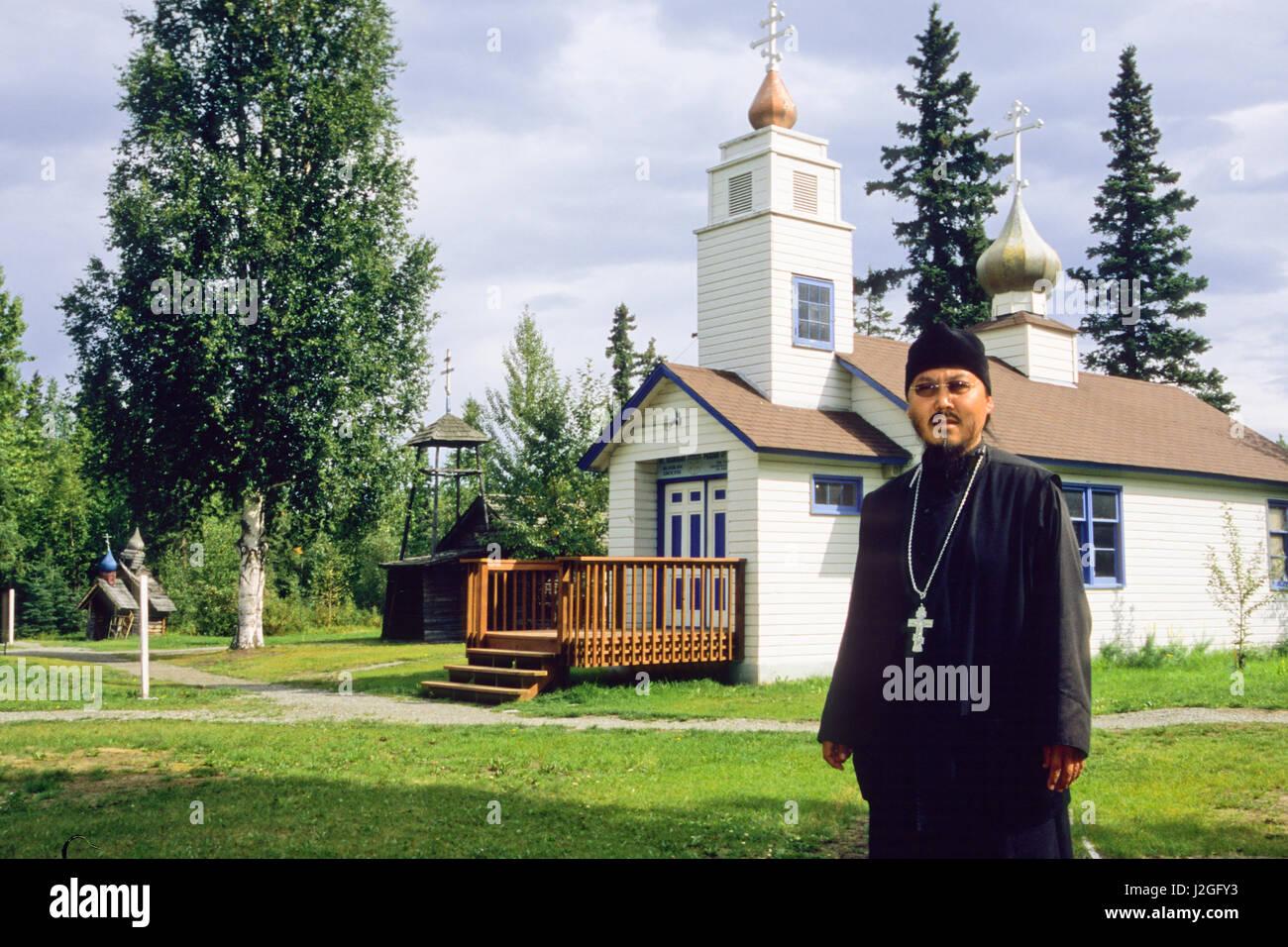 Alaskan Native man dressed in black robes of the parish stands in front ...