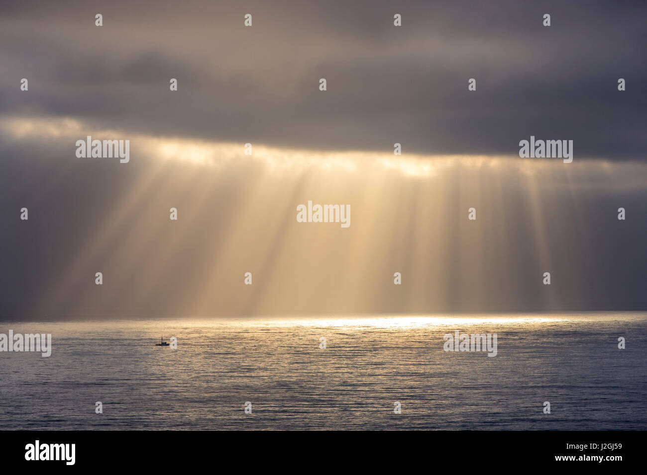 Rays emit from the clouds over the Pacific Ocean as fishing boat passes ...