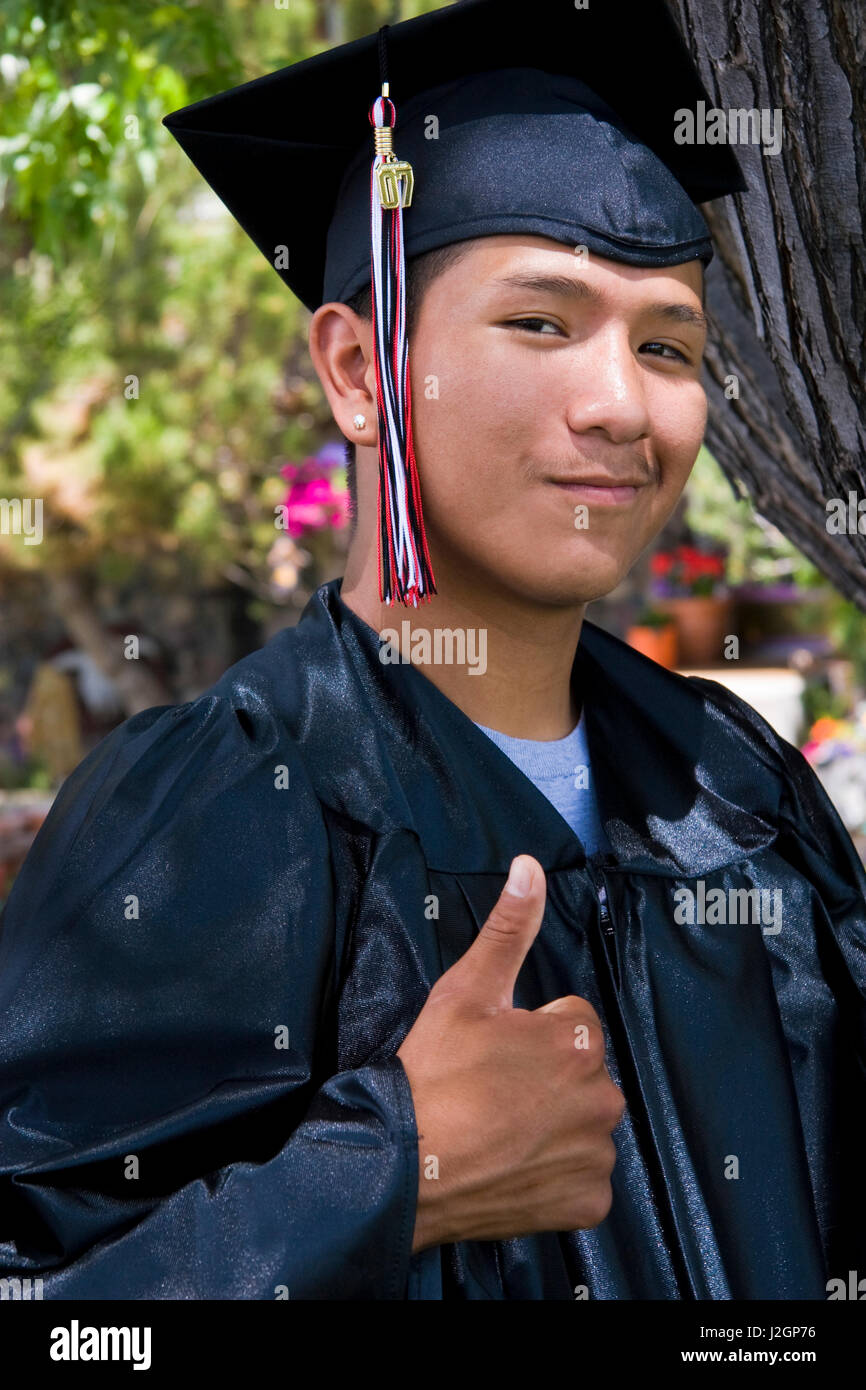 Native American young man dressed in cap and gown gives a thumbs up ...