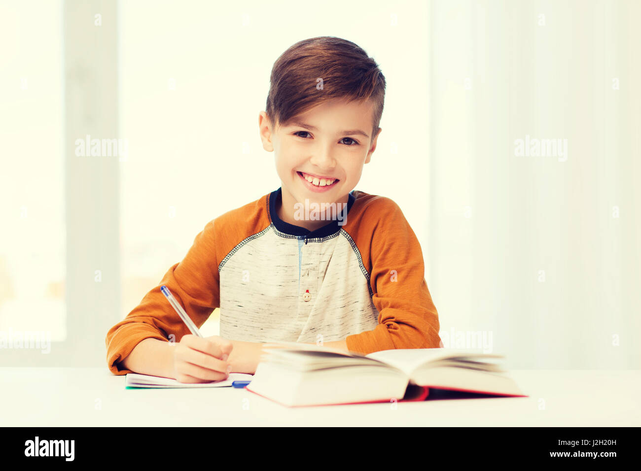 smiling student boy writing to notebook at home Stock Photo - Alamy