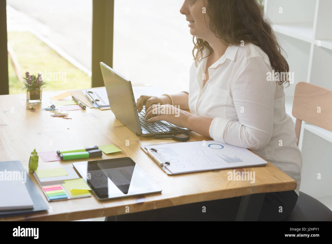 Young female woman entrepreneur sitting and working at a desk typing on ...