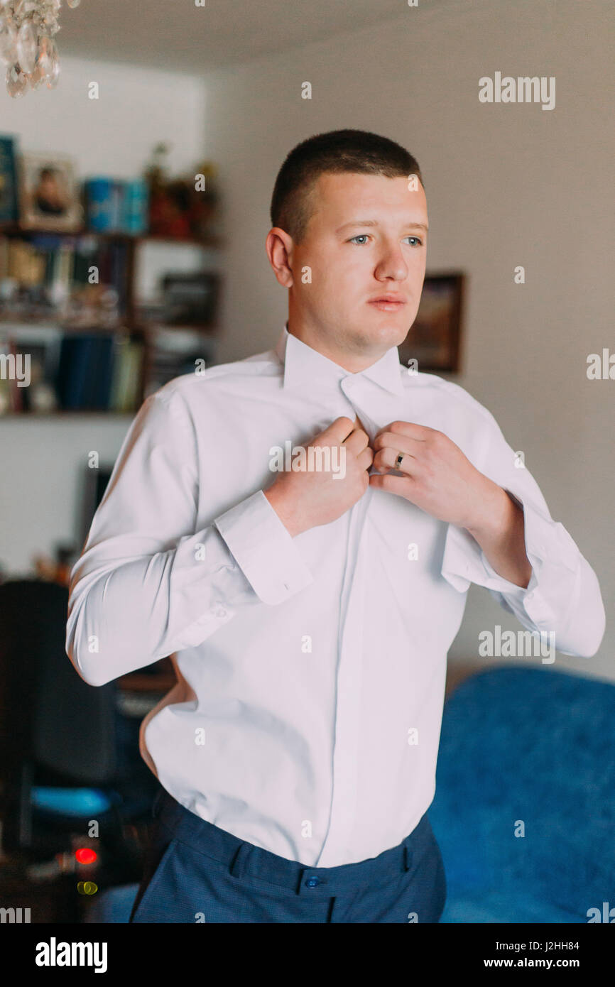 Young groom wears white shirt, dressing himself for wedding ceremony ...