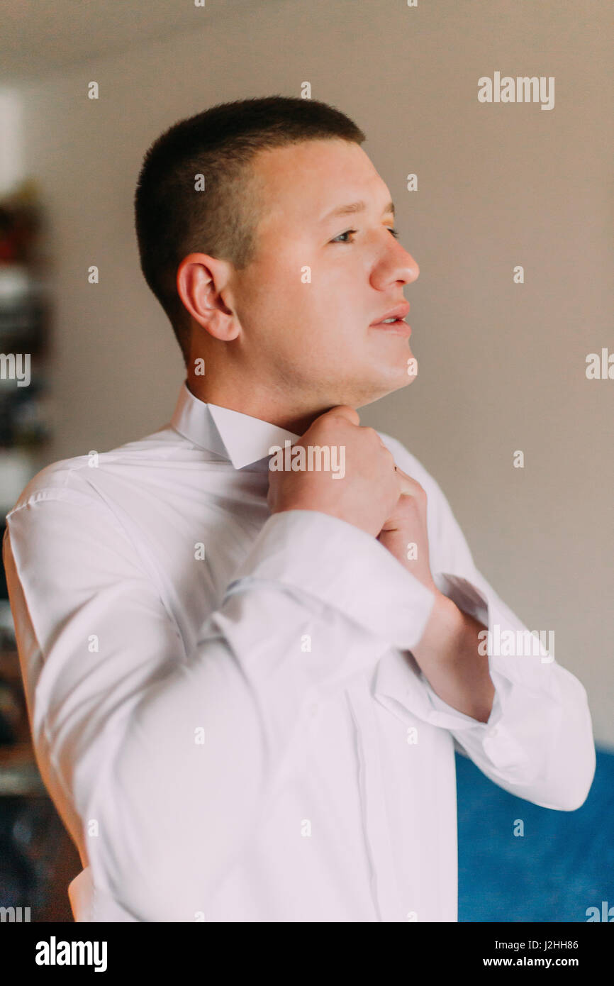 Young groom fixing collar when dressing himself for wedding ceremony ...