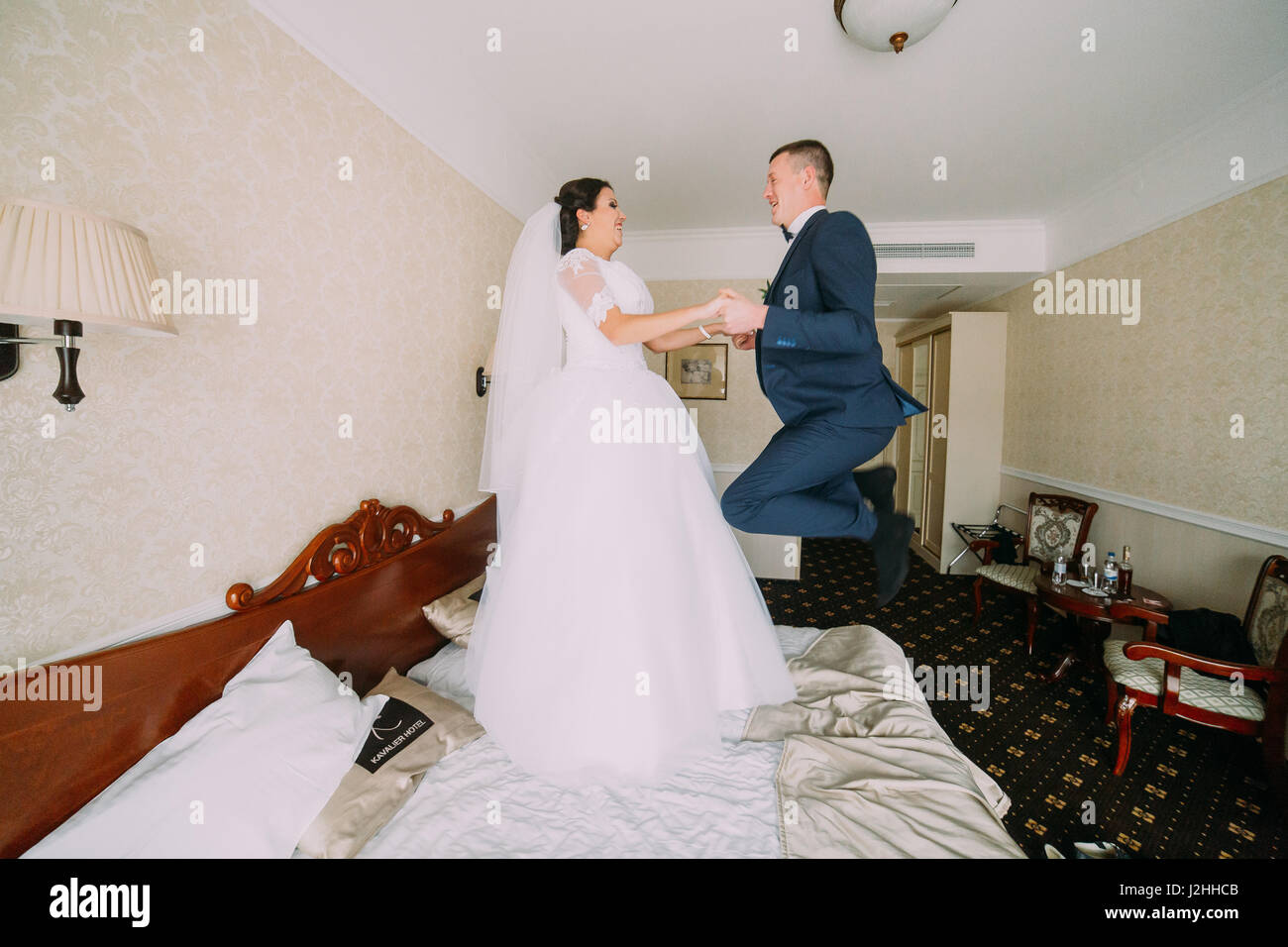 Happy bride and groom in a hotel room playfully jumping on bed. Honeymoon concept Stock Photo ...