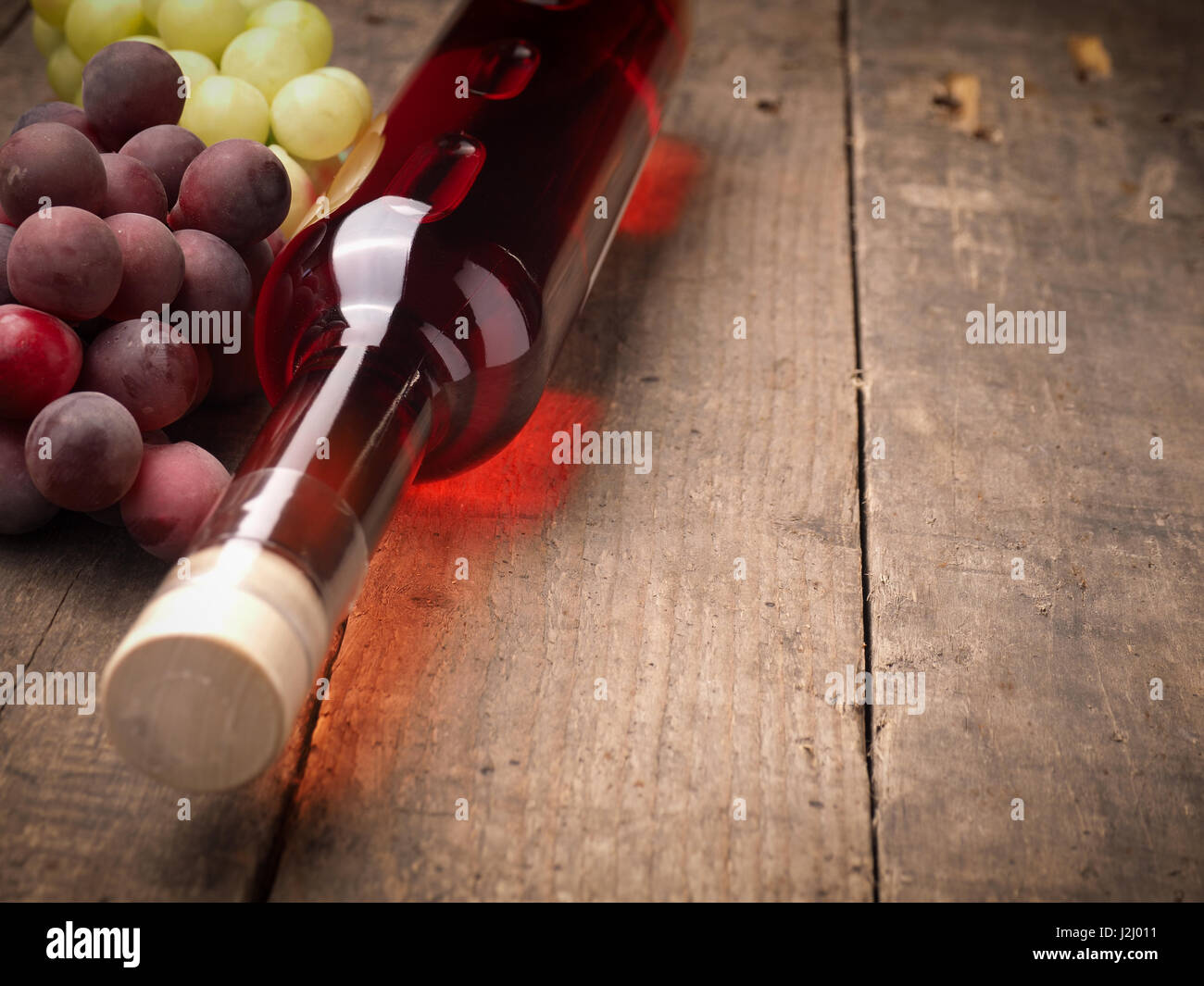 Bottle of red wine with grapes on a rustic wooden table with space for ...