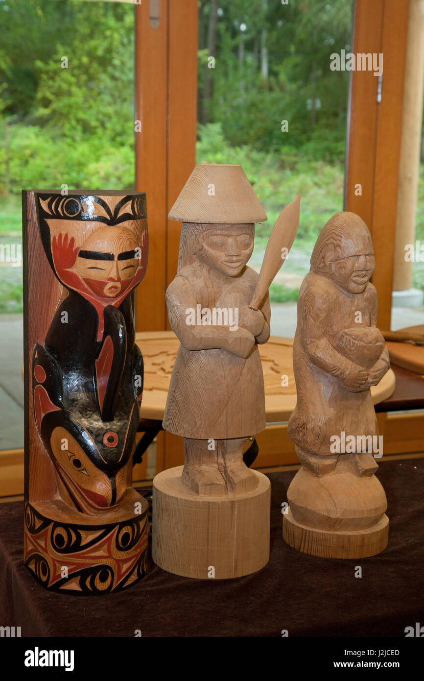 Miniature scale carved wooden totems are made before a larger totem ...