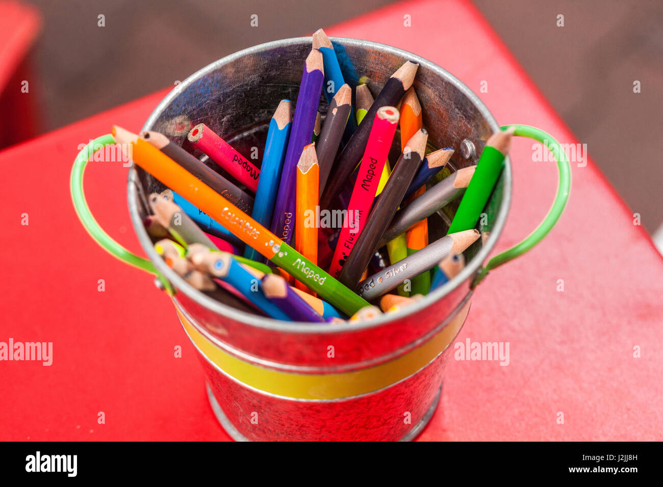 Multicolored pencils in pot, bucket on a red table Stock Photo - Alamy