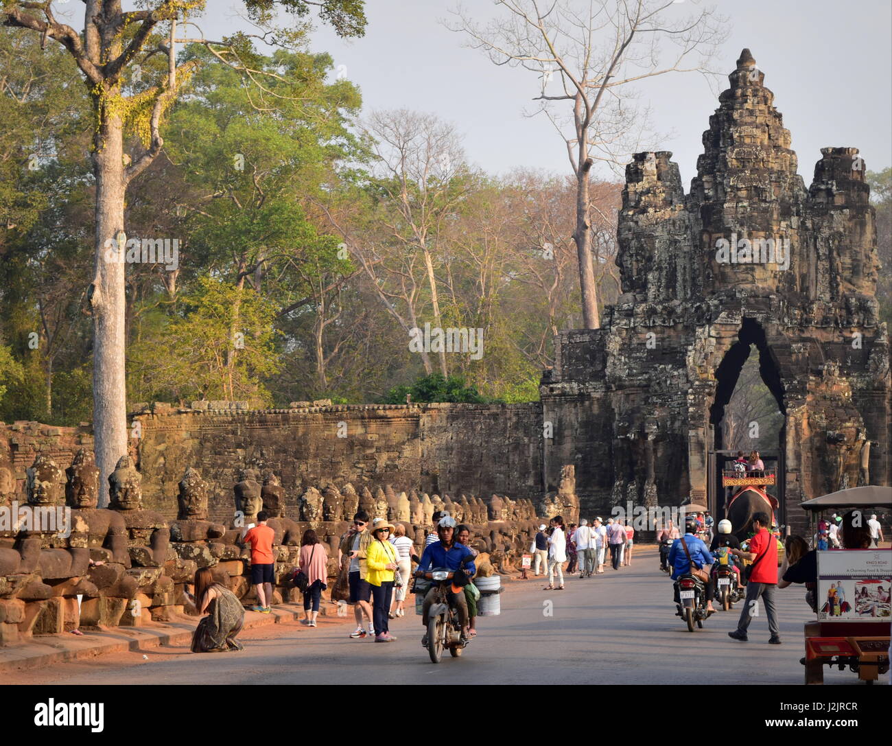 Tourists walk along the pathway to Angkor Thom ancient ruins gate ...