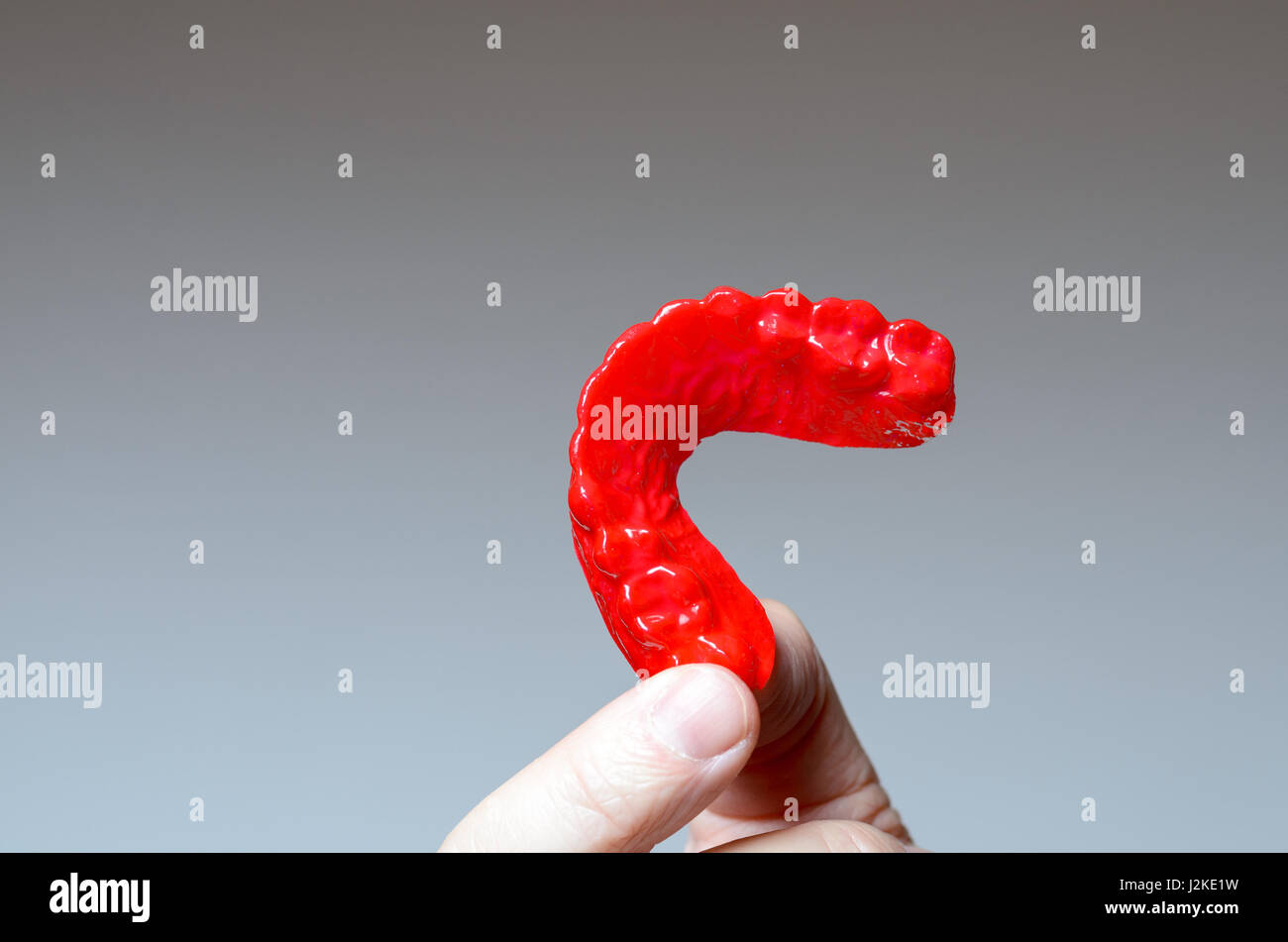 Finger holding a red bite plate to protect his teeth at night from ...
