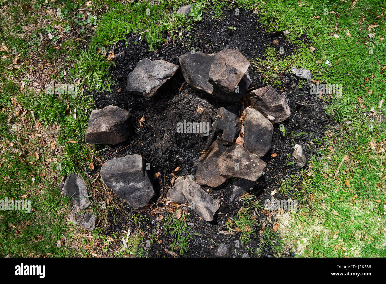 top view of extinguished campfire place with grass stones and black ...