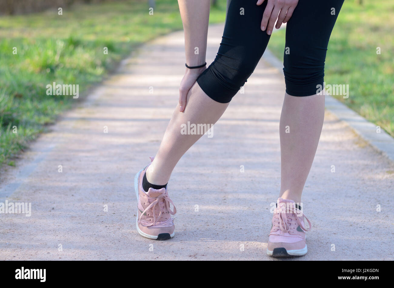 Young woman jogger suffering from calf muscle spasm or cramps bending ...