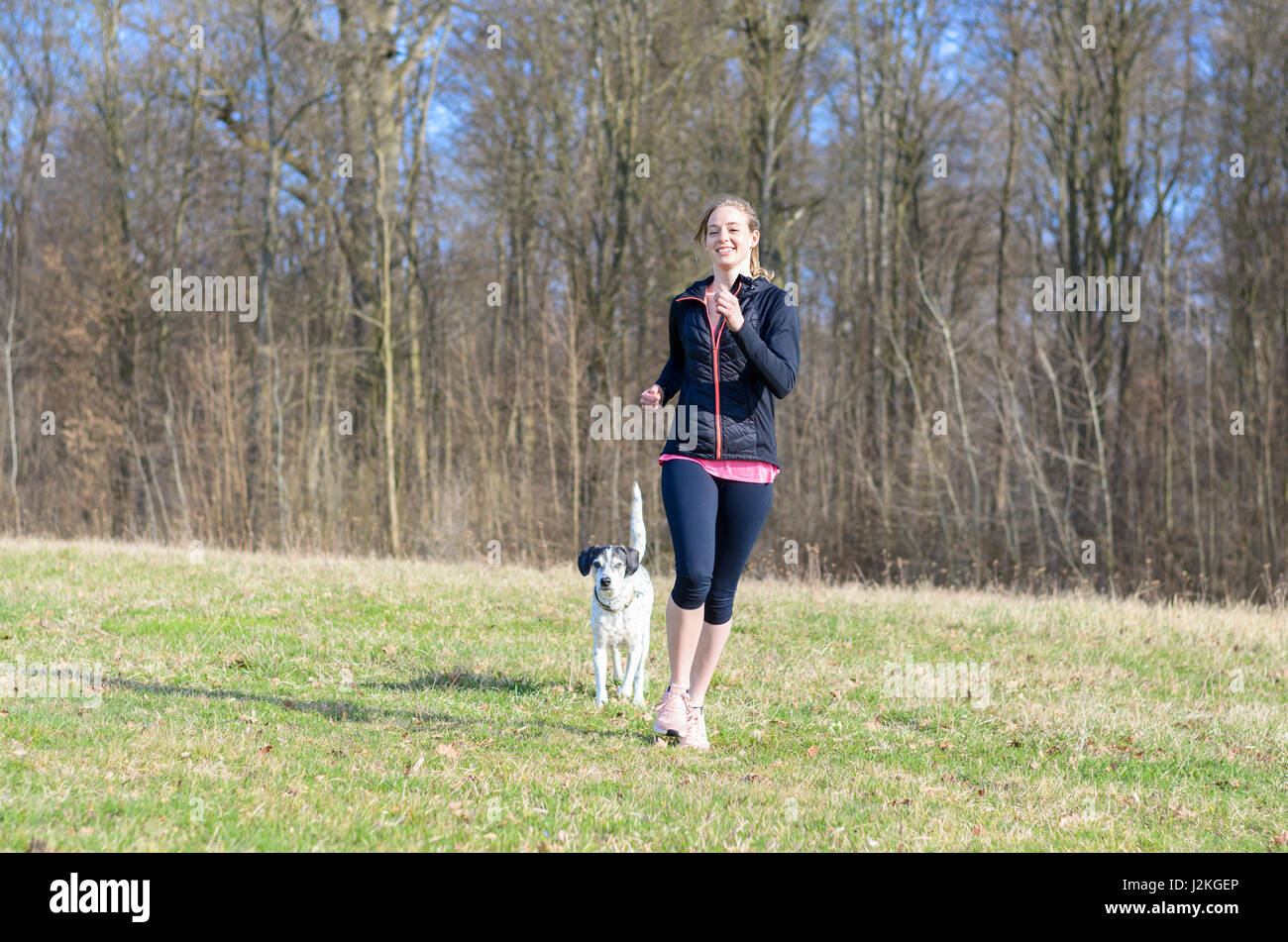 Fit young woman out jogging with her dog running through a rural field ...