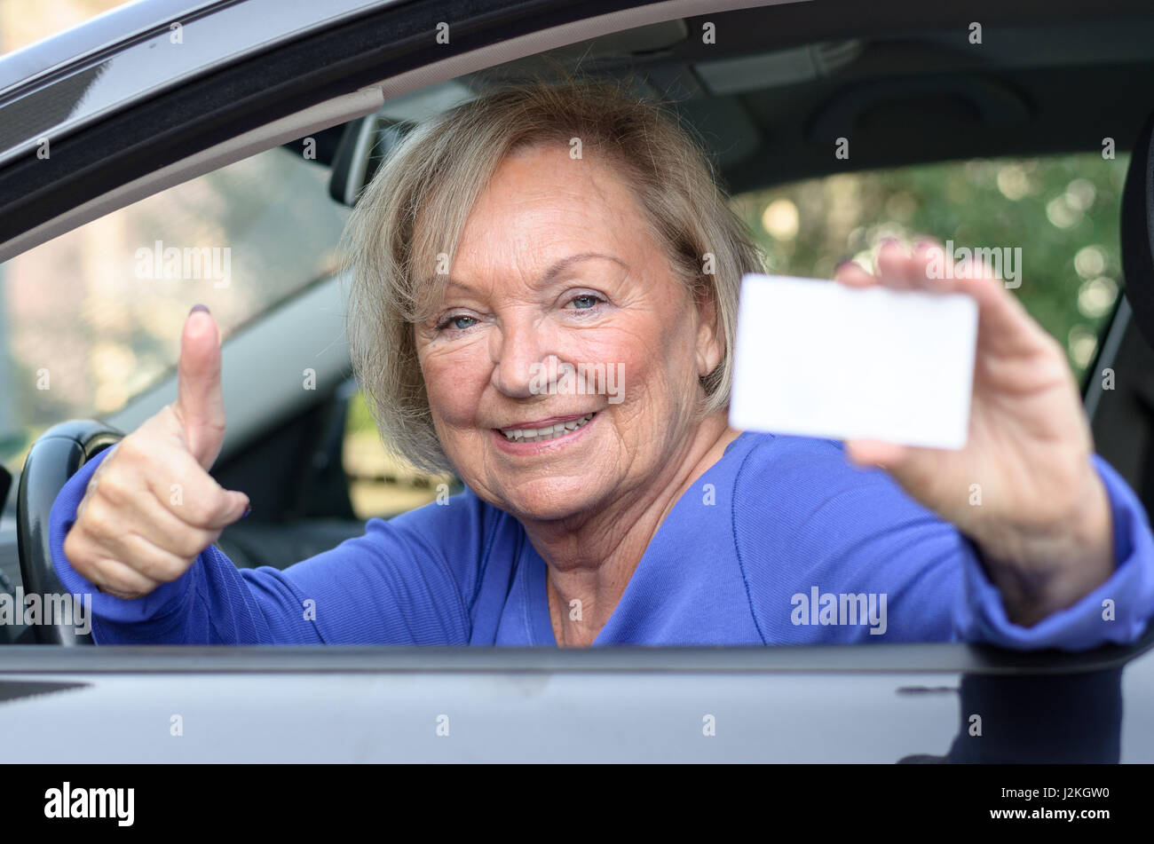 Happy elderly woman showing off her drivers licence as she leans out of ...