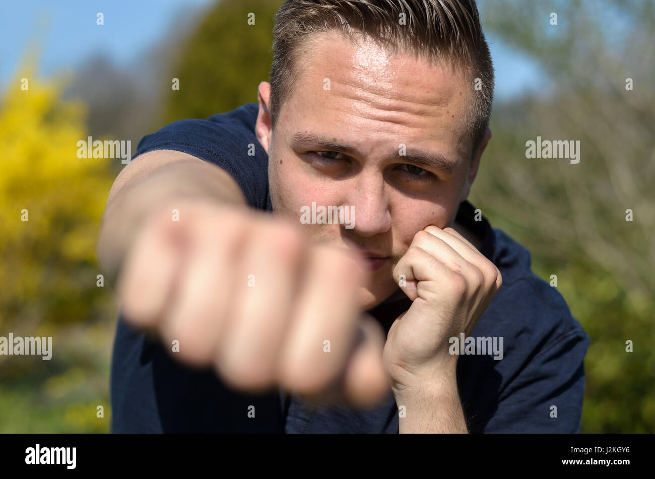 Determined young man punching at the camera with his clenched fist with ...