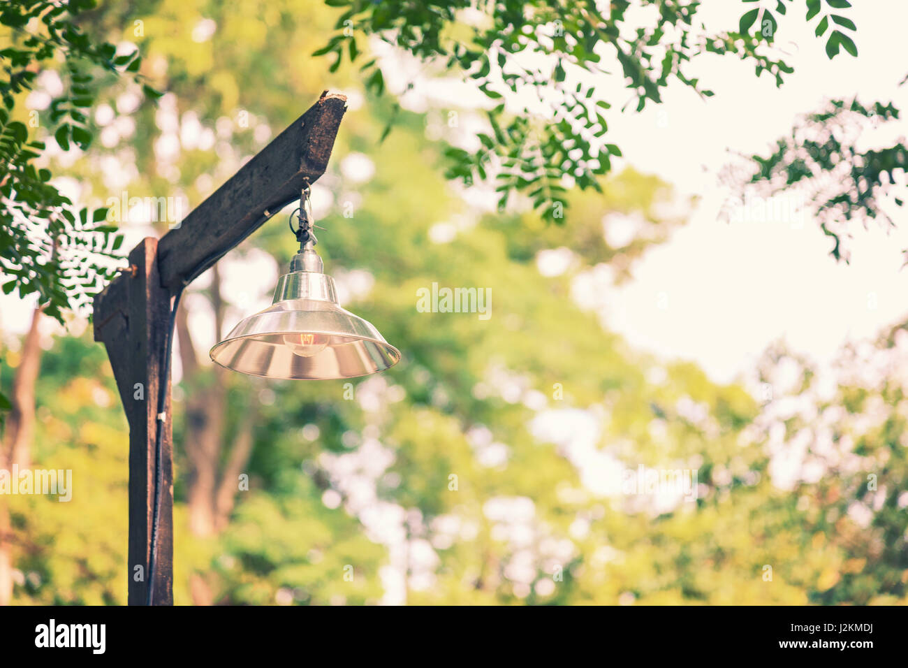simple basic lamp on old rustic wooden lampost against blurred trees ...