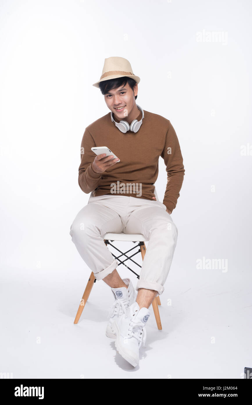 Smart casual asian man seated on chair, holding smartphone in studio ...