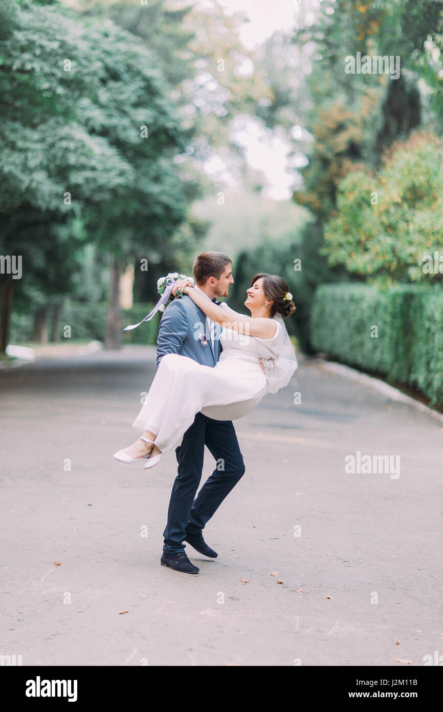 Beautiful wedding couple portrait with groom carrying his smiling bride ...
