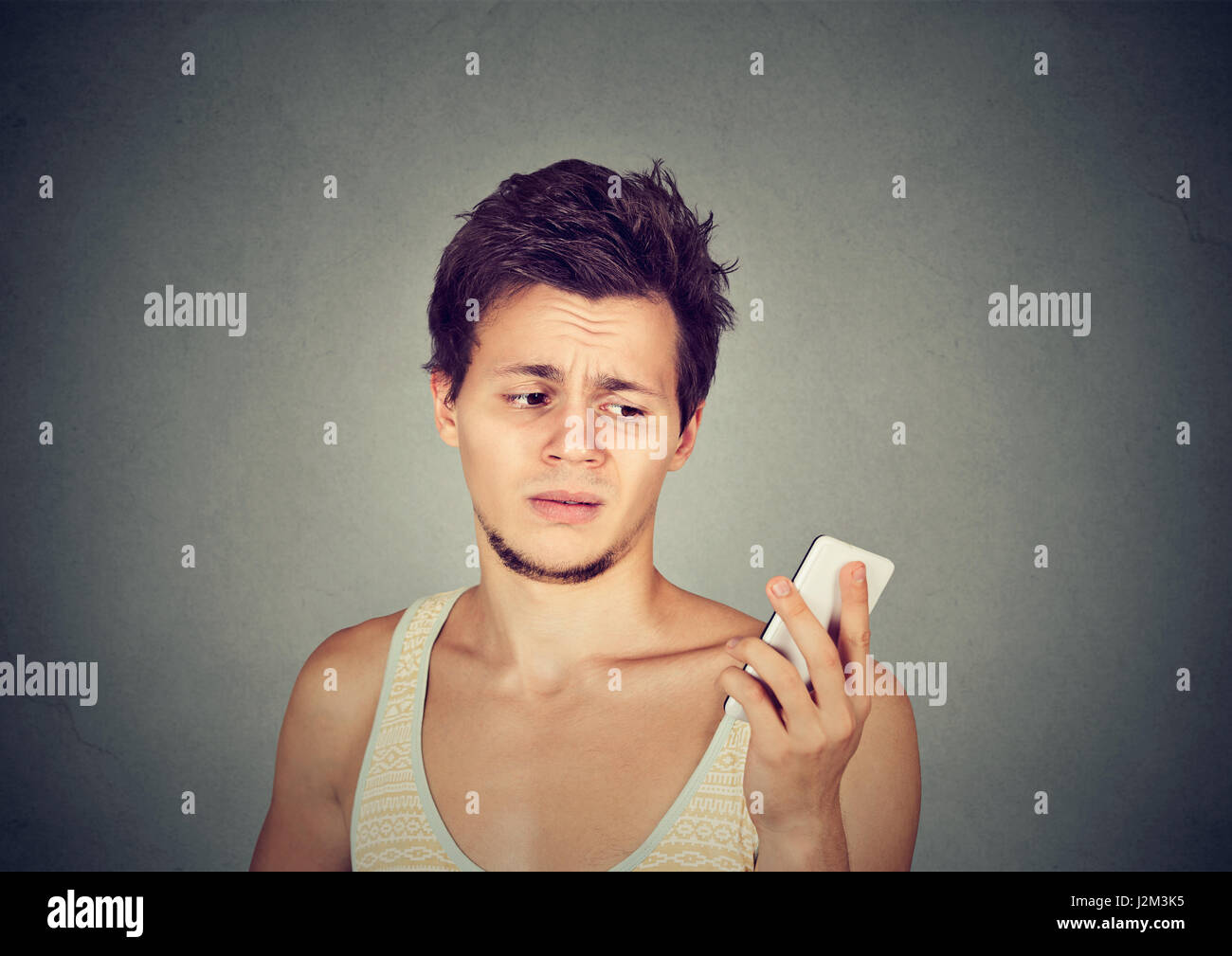 Portrait of annoyed young man holding cellphone in hands looking at ...