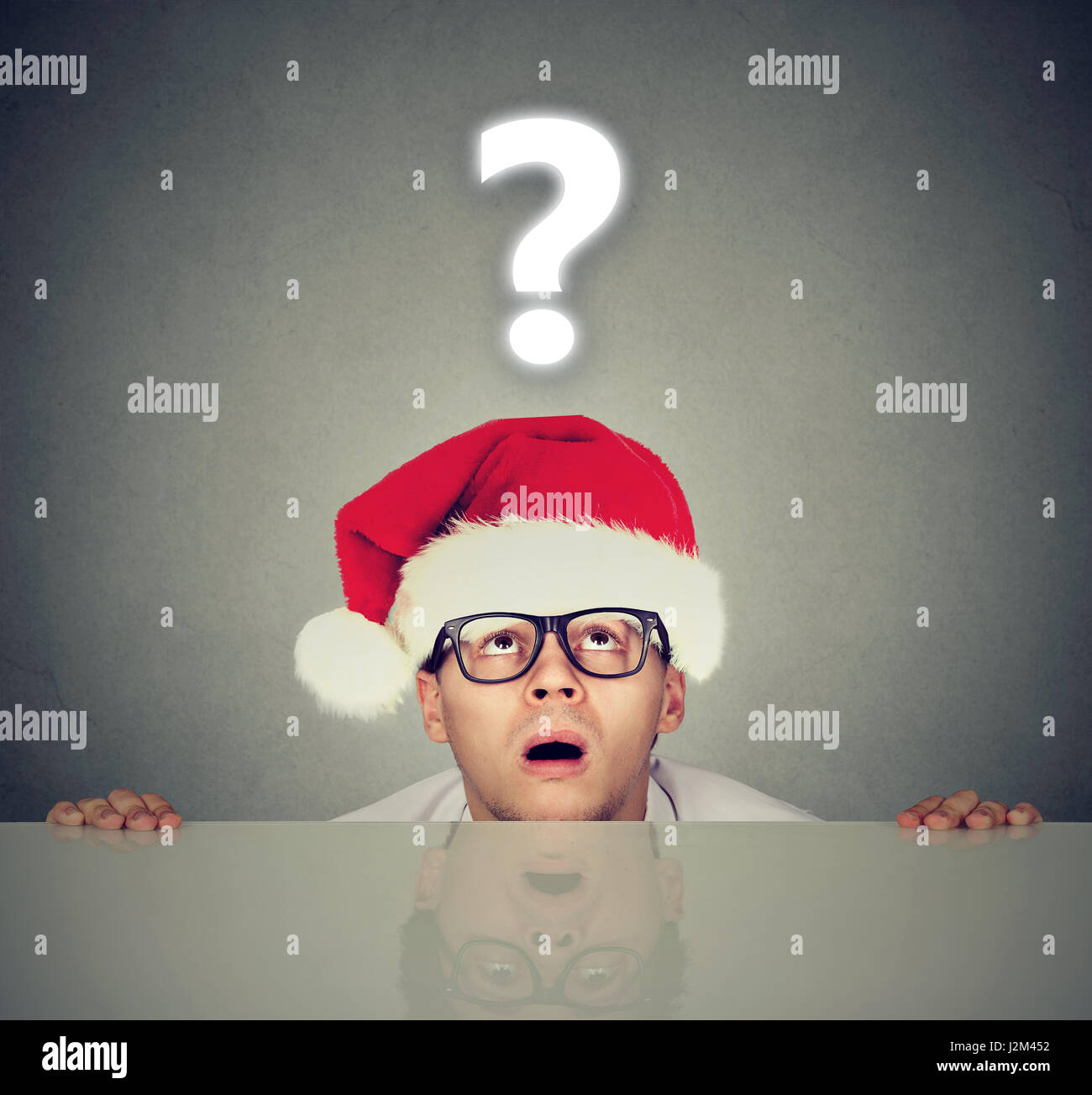 Young man in santa claus hat with question mark wondering about ...