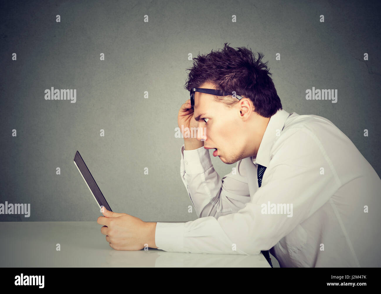 Side profile shocked young man looking at his laptop computer sitting ...