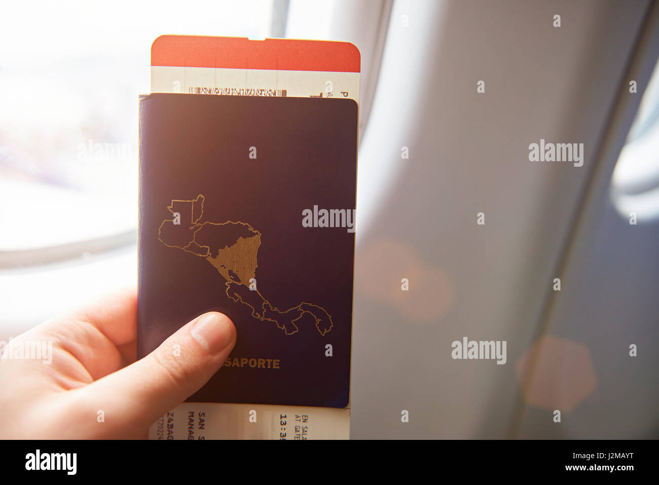Hand holding passport with flight ticket close up on plane window ...