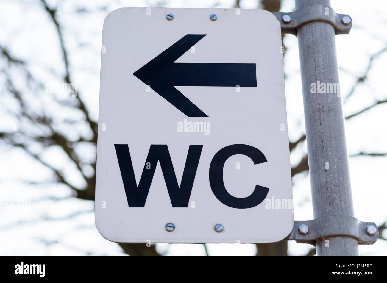 Close-up of white WC sign with black letters and left arrow on pillar ...