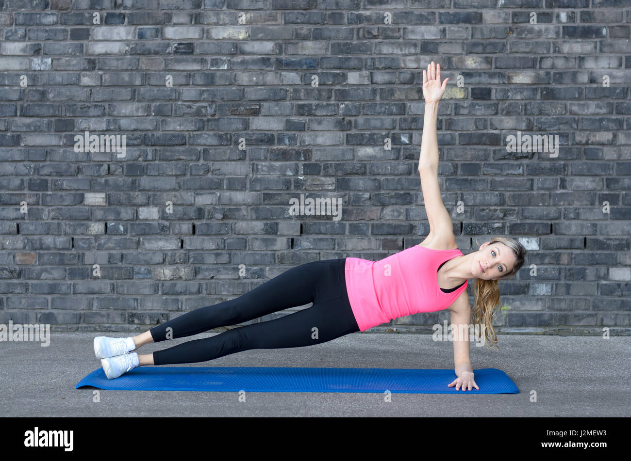 Smiling beautiful woman in pink top and black pants doing plank ...