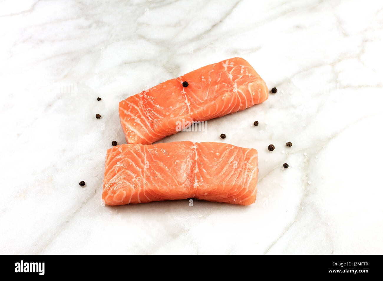 A photo of two slices of salmon on a white marble table with a place ...