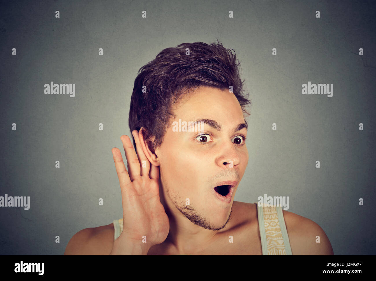Handsome, young, nosy, shocked man with hand to ear gesture, carefully ...