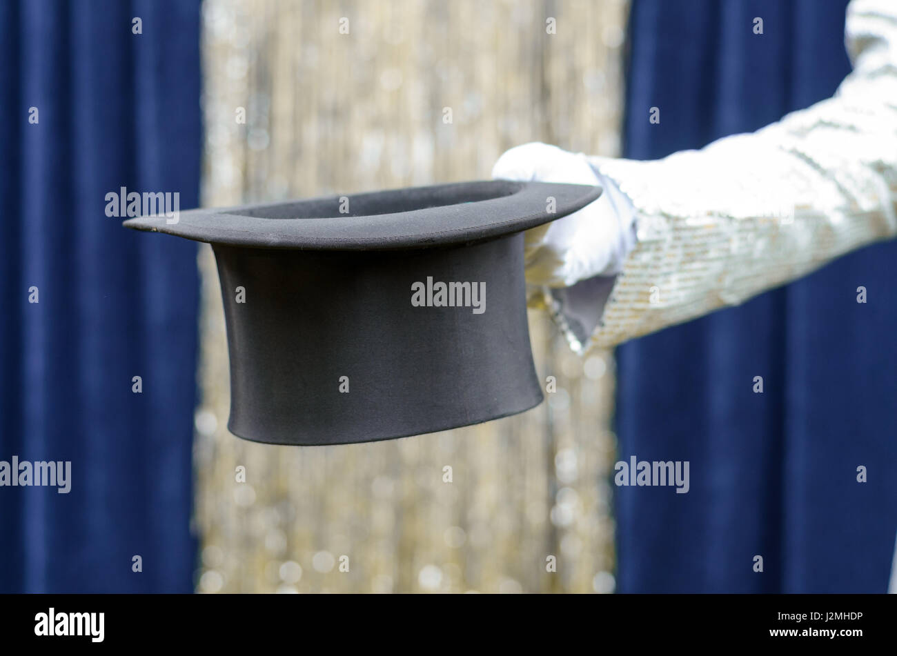 Gentleman or magician holding out a top hat in his gloved hand in front ...