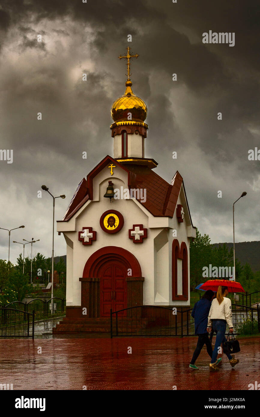 Orthodox Church against the dramatic sky on rainy day. People walk ...