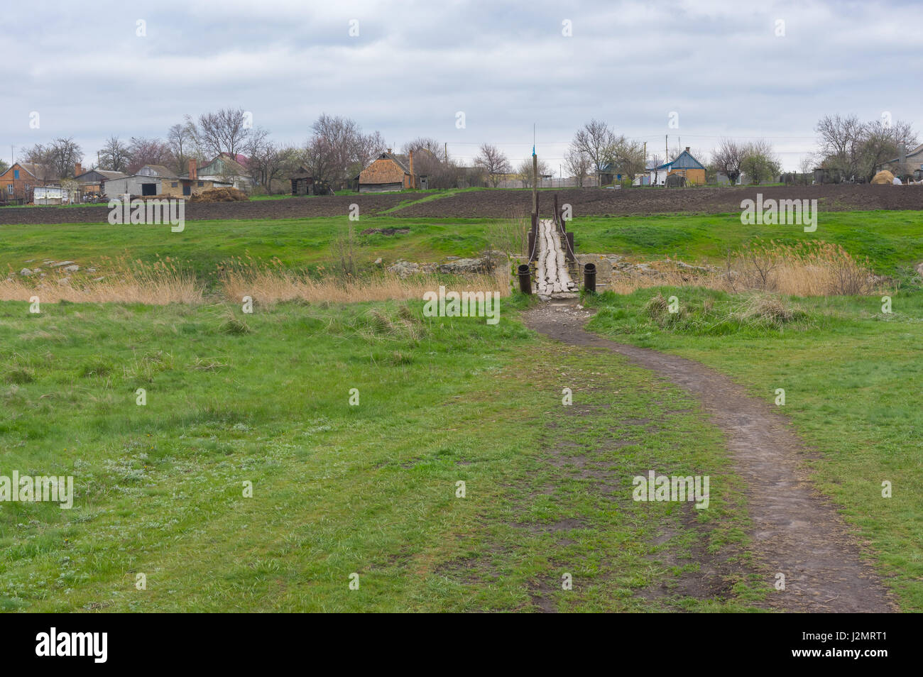 Pedestrian path through spring meadow to old foot-bridge over small ...