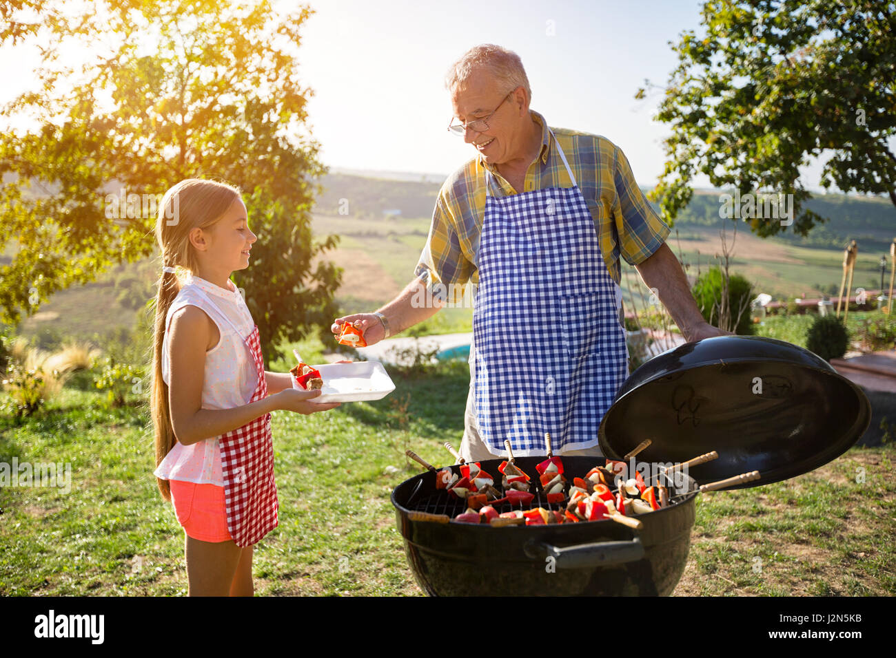 smiling grandfather and granddaughter making barbecue in countryside ...