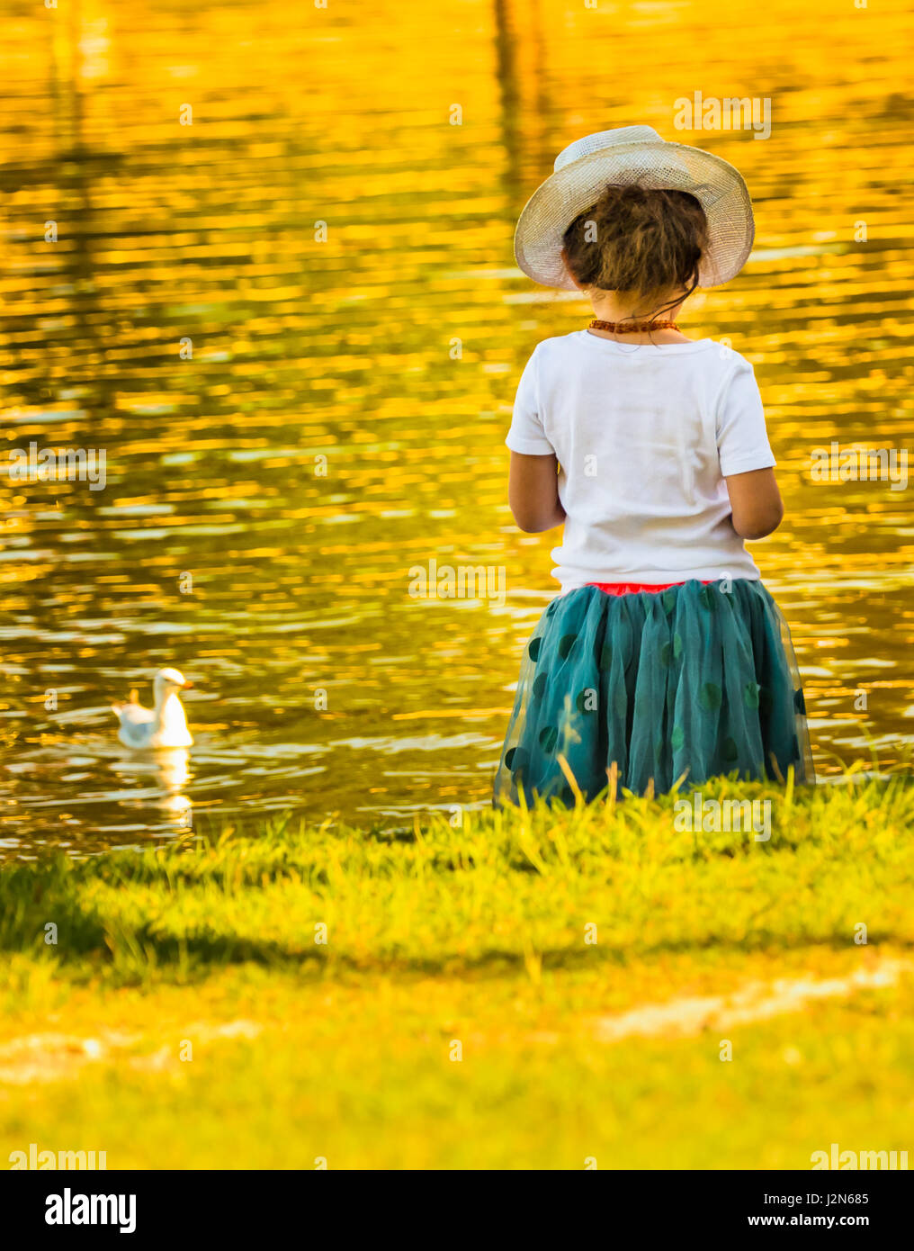 Girl standing with a hat standing in front of water looking down ...